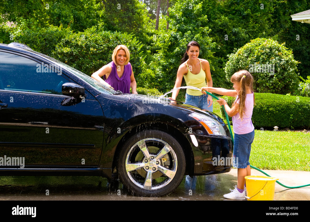 Child and mother and friend having fun at home washiong car together ...
