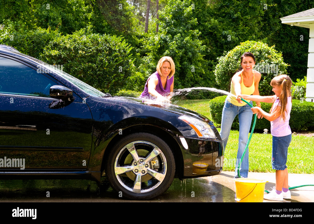 Child and mother and friend having fun at home washiong car together ...