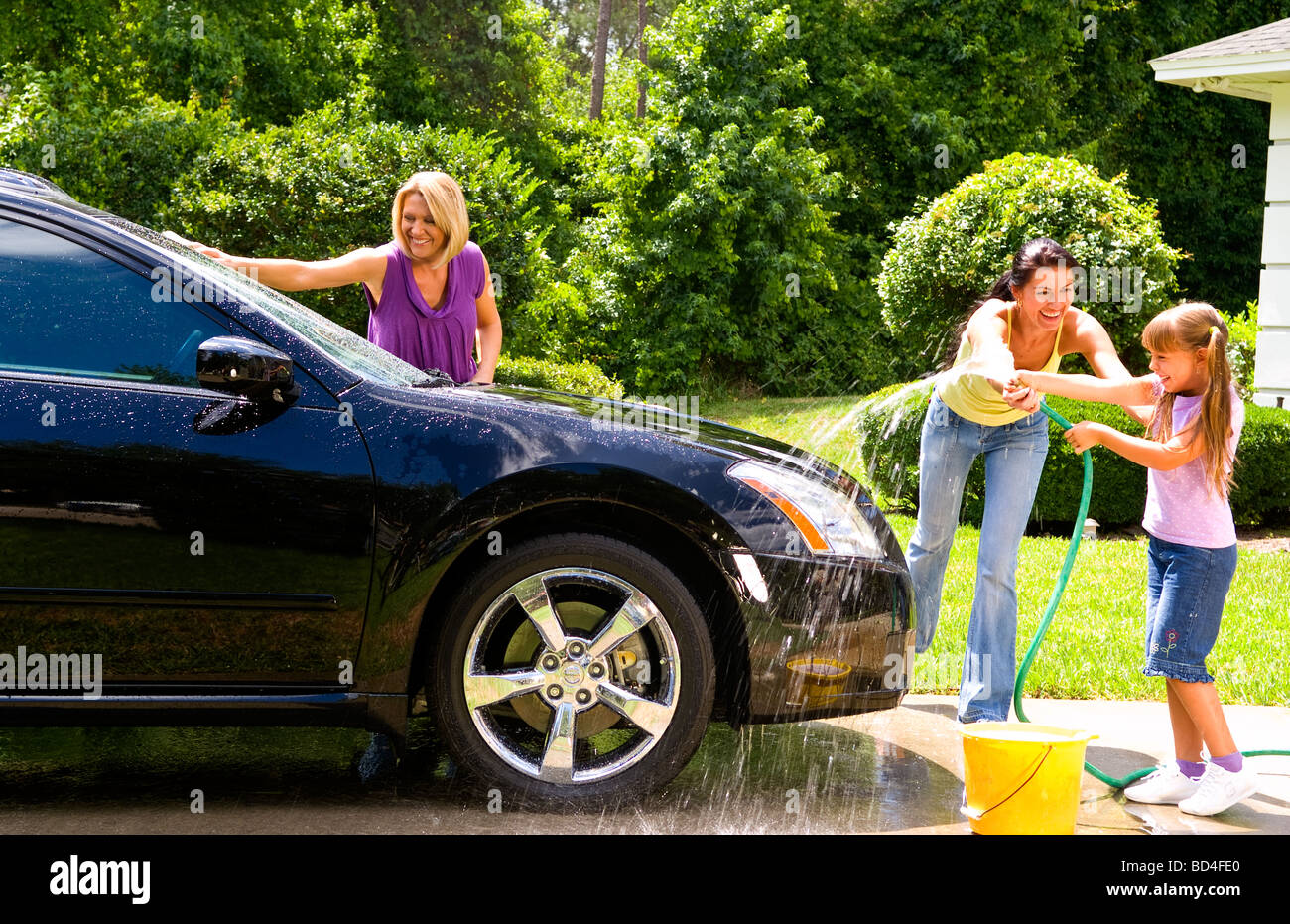 Child and mother and friend having fun at home washiong car together ...