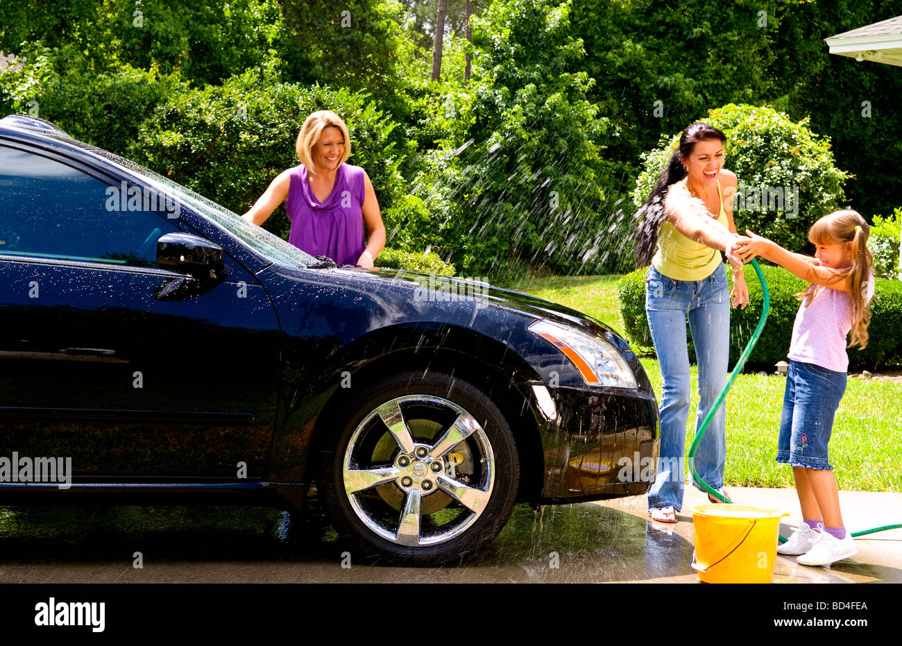 Child and mother and friend having fun at home washiong car together ...