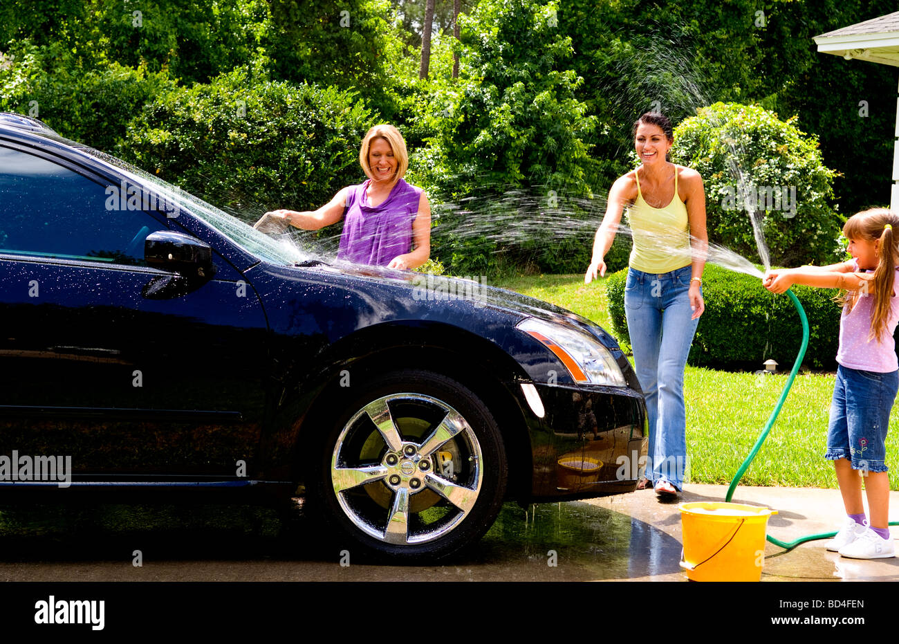 Child and mother and friend having fun at home washiong car together ...
