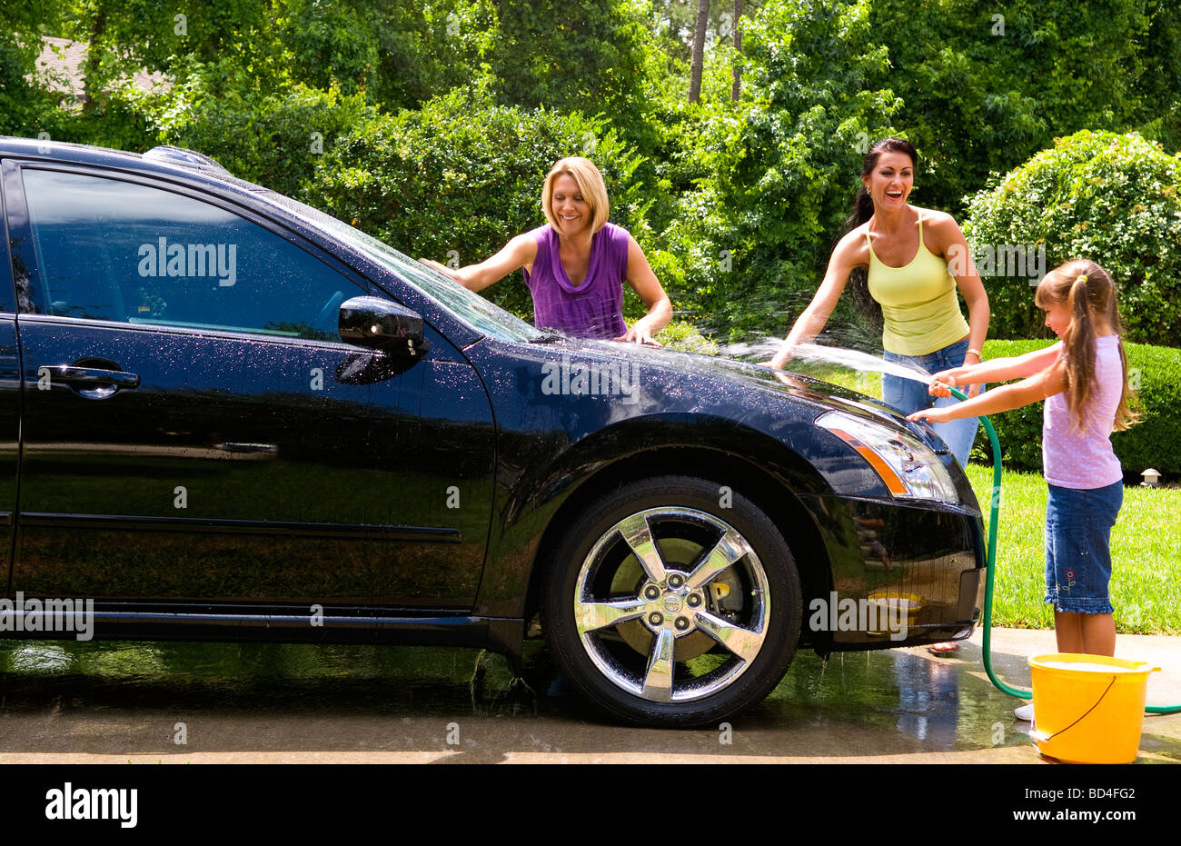 Child and mother and friend having fun at home washiong car together ...