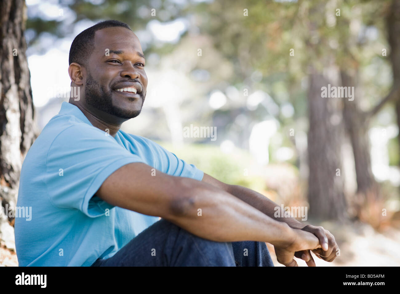 A man sitting outdoors by a tree Stock Photo - Alamy