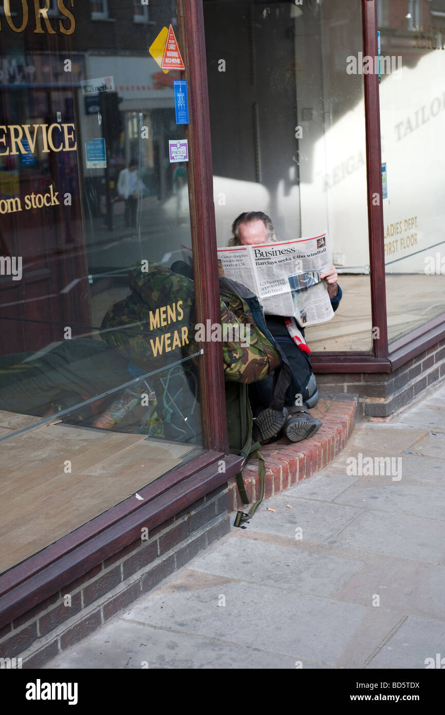Old (tramp) man sitting in a shop doorway reading the financial pages ...