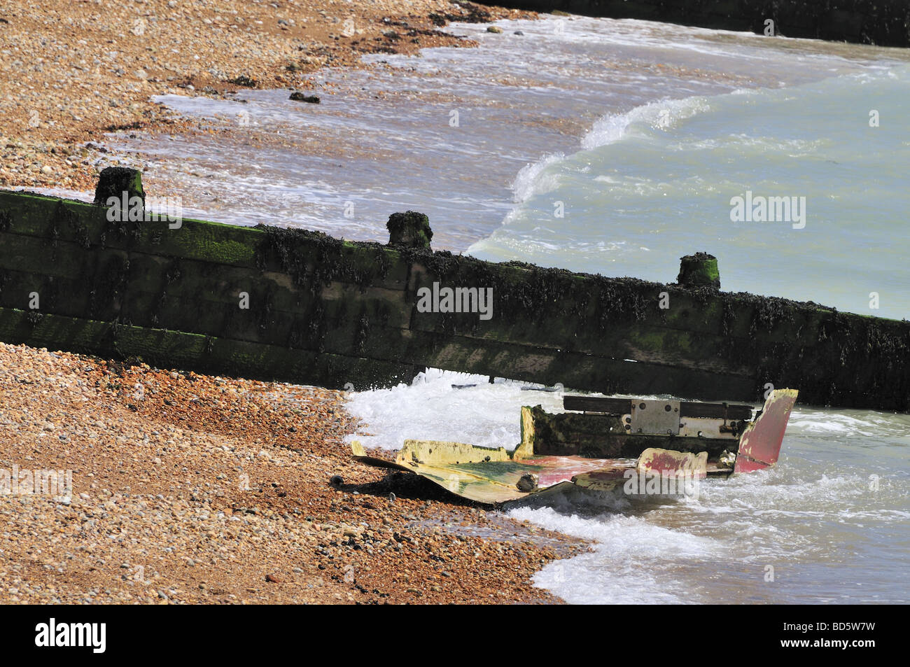 Small wrecked rowing boat,washed up on the shingle next to a wooden ...