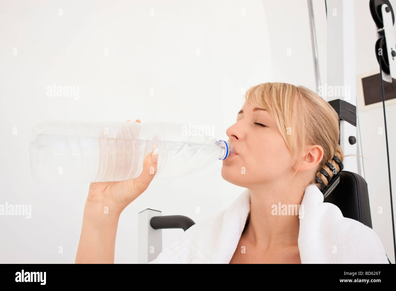 Young blond Caucasian woman workout in gym. Model holds bottle with ...