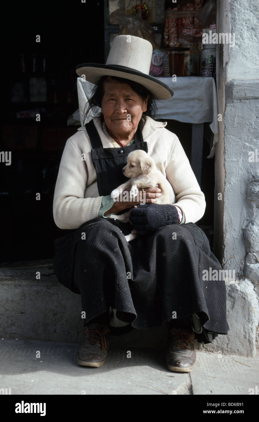 Woman shopkeeper sitting on step outside shop holding puppy, Potosi ...