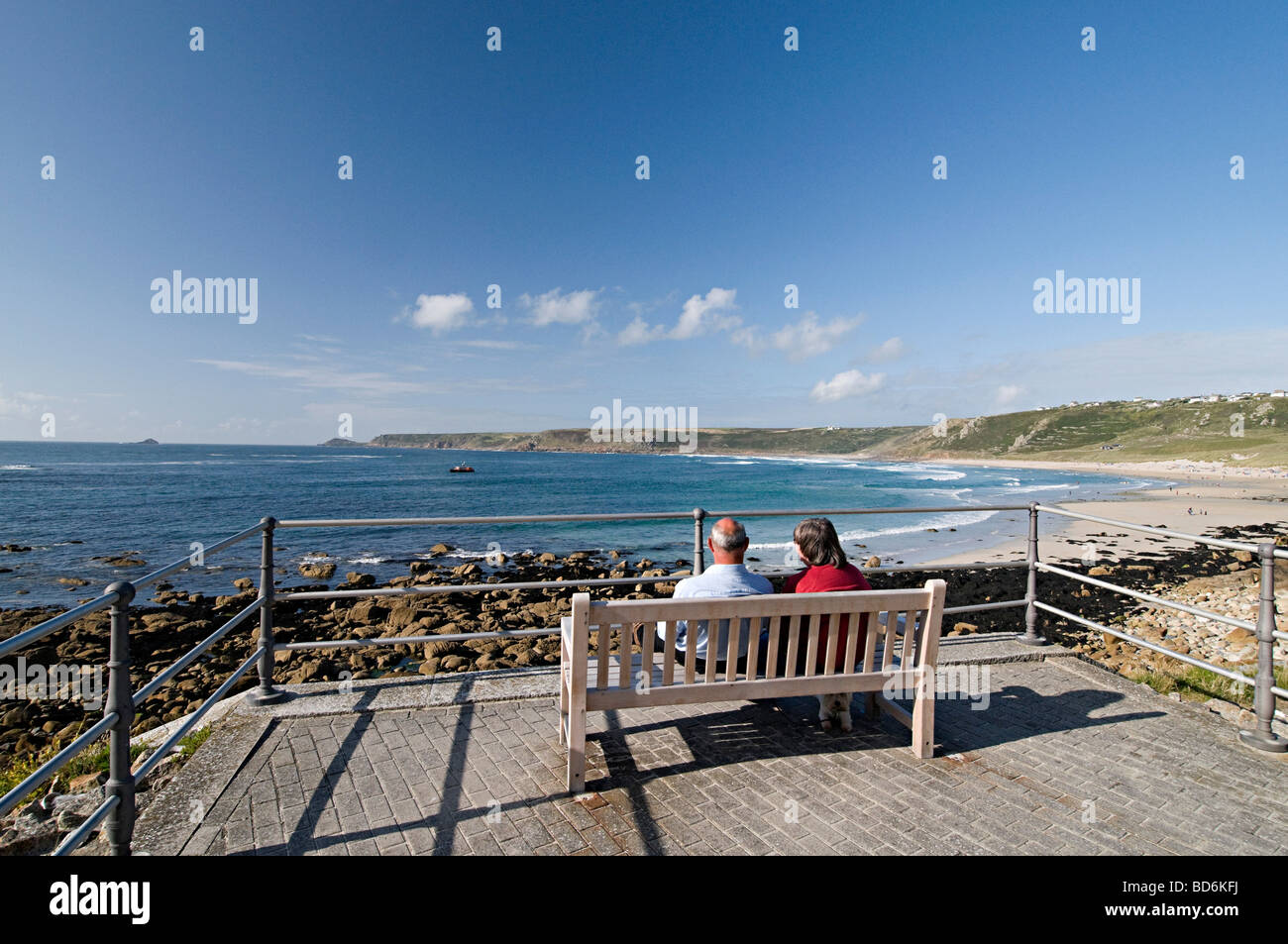 a couple sitting on a bench looking out to sea in sennen cove cornwall ...