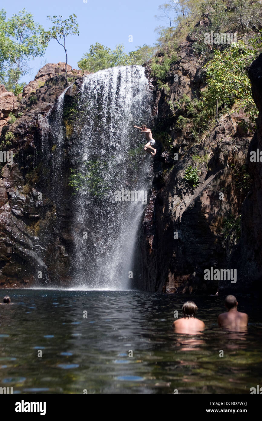 People watch a man jump off a rock face into a pool of water in front ...