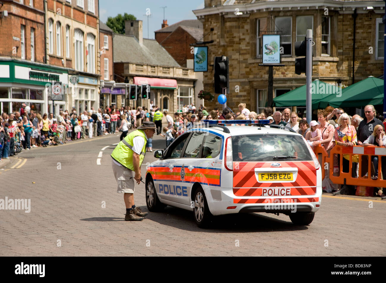 Crowds of people waiting behind a barrier as a police car passes ...