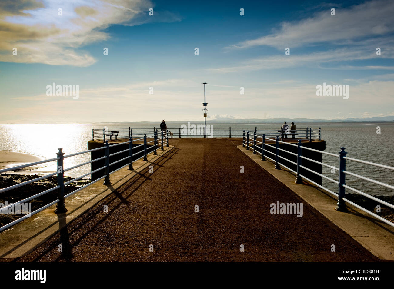 Silhouetted figures at the end of Stone Jetty, Morecambe Bay at sunset ...