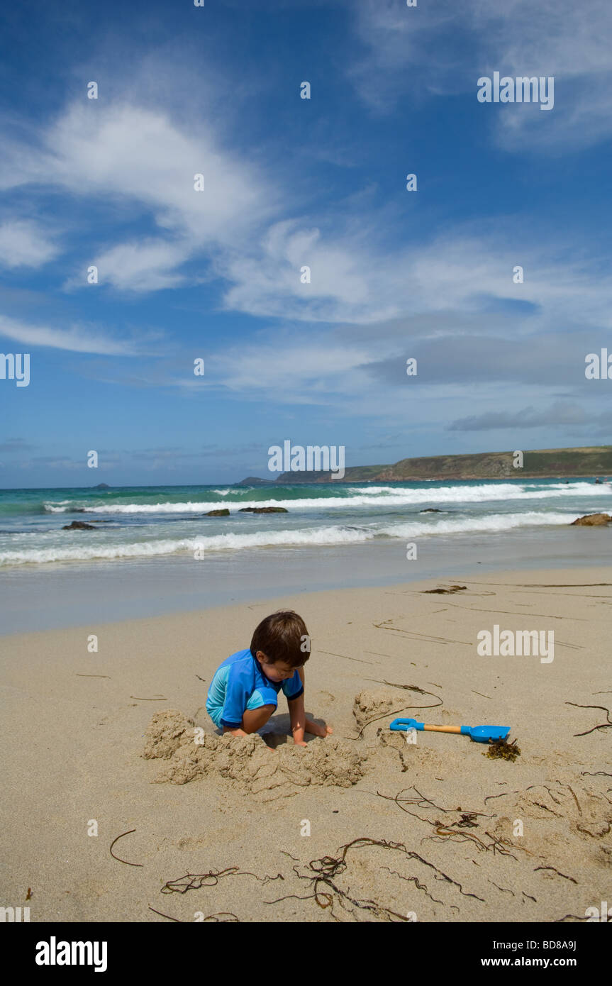 A six year old boy in a sunsuit plays in the sand at Sennen Cove beach ...