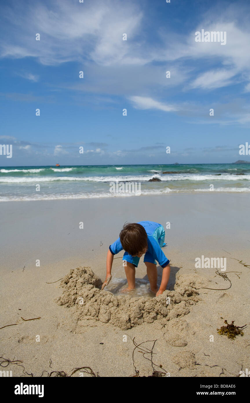A six year old boy in a sunsuit plays in the sand at Sennen Cove beach ...