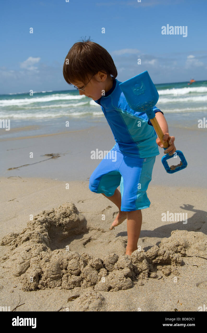 A six year old boy in a sunsuit plays in the sand at Sennen Cove beach ...