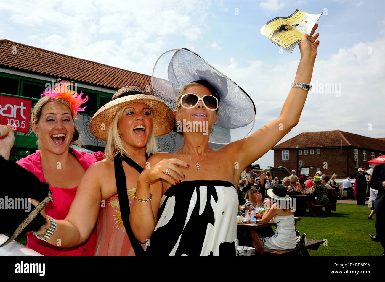 Racegoers in glamorous outfits and hats cheer on the runners and riders ...