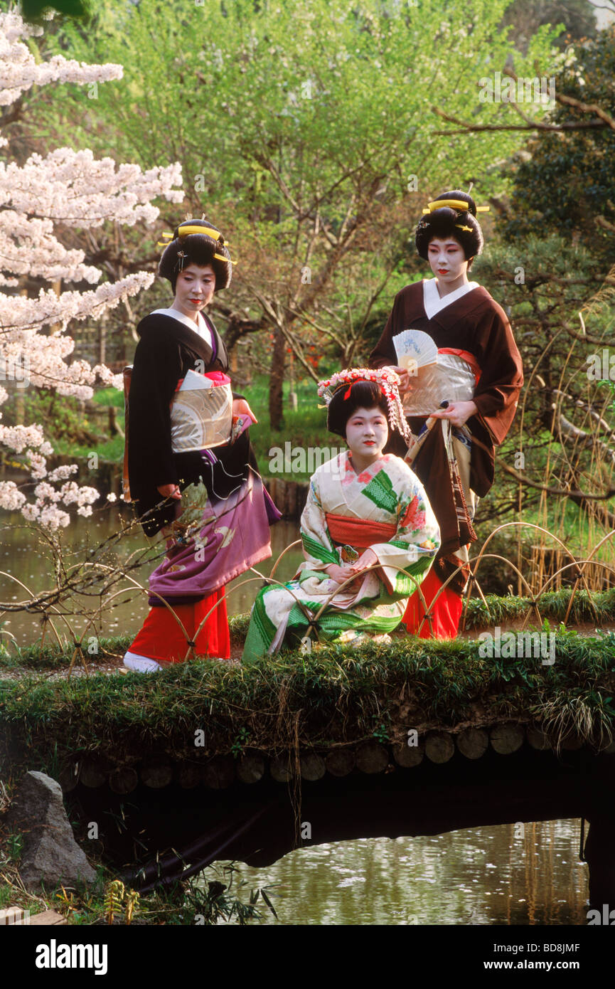 Three Geisha women in colorful kimonos in Tokyo park on bridge over ...