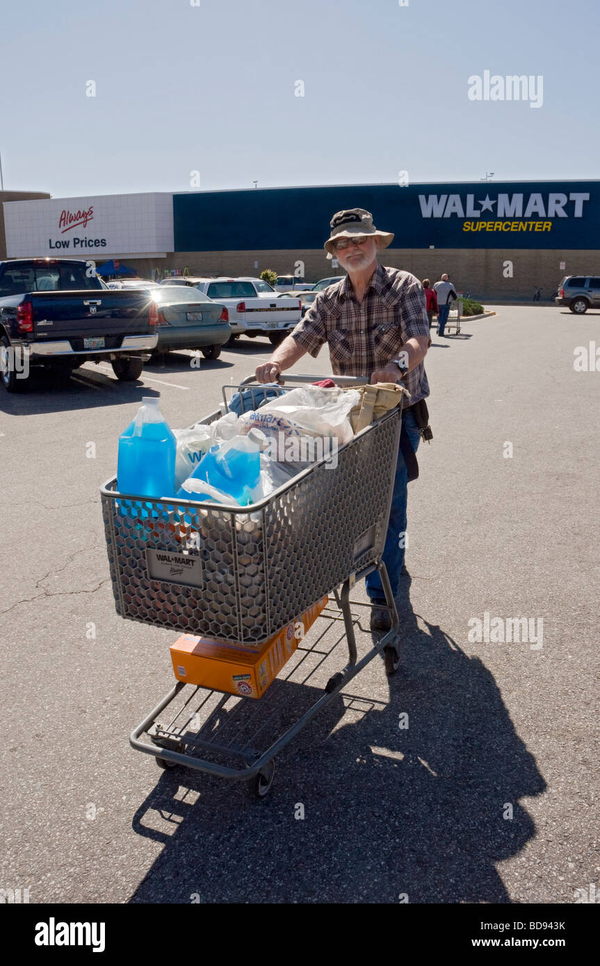 older man with shopping cart full of items in parking lot of Wal Mart ...