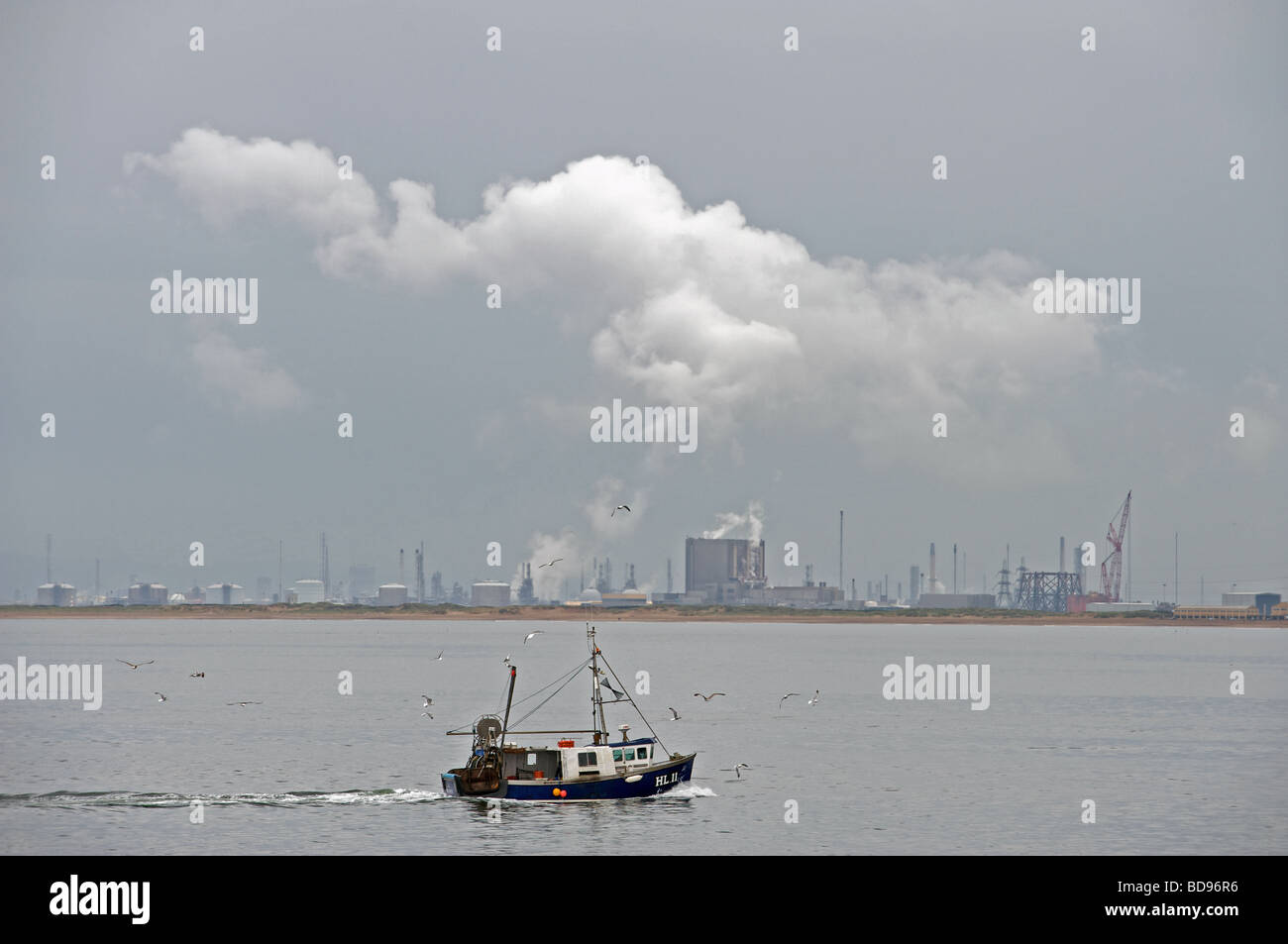 Fishing boat sailing past a nuclear power station and oil refinery ...
