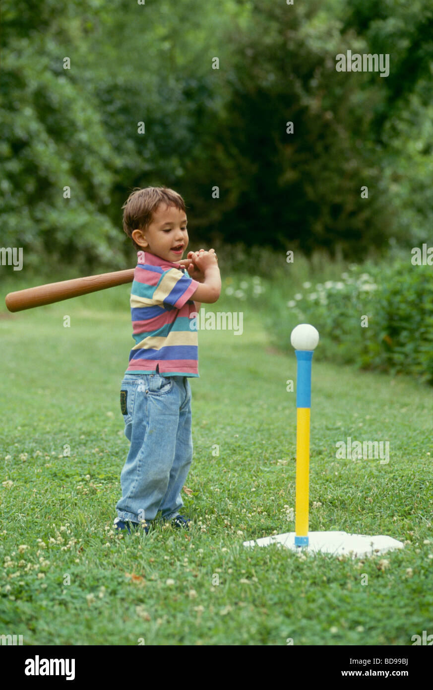 Afghan American boy aims his bat while playing T-ball in grassy field ...