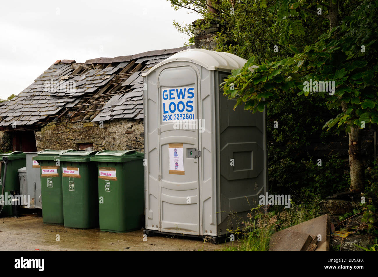 Temporary toilet and green wheelie bins in front of derelict building ...