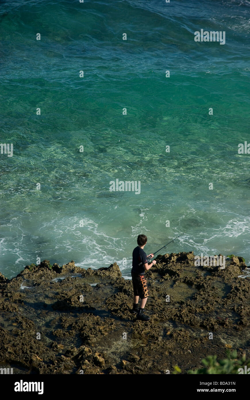 Boy fishing in ocean from a rocky outcrop Stock Photo - Alamy