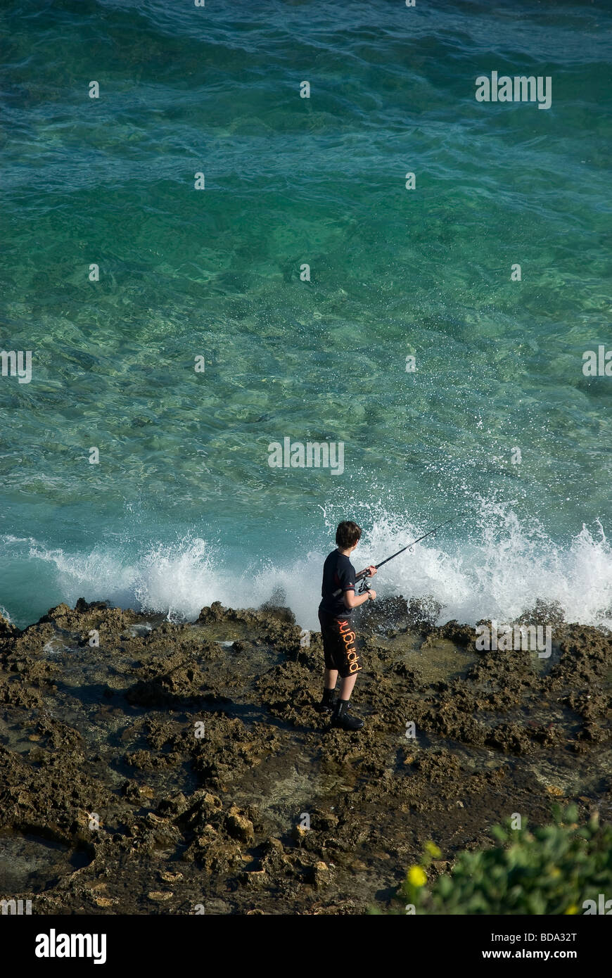Boy fishing in ocean from a rocky outcrop Stock Photo - Alamy