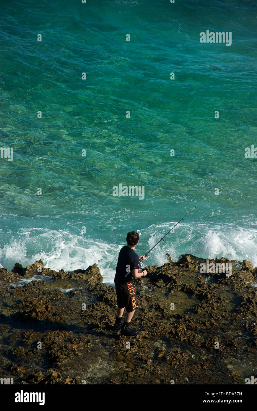 Boy fishing in ocean from a rocky outcrop Stock Photo - Alamy