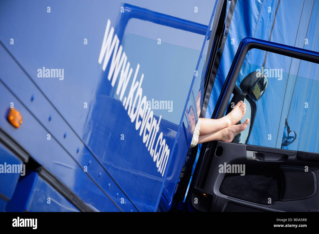 A lorry driver rests his bare feet on the cab door of his truck ...