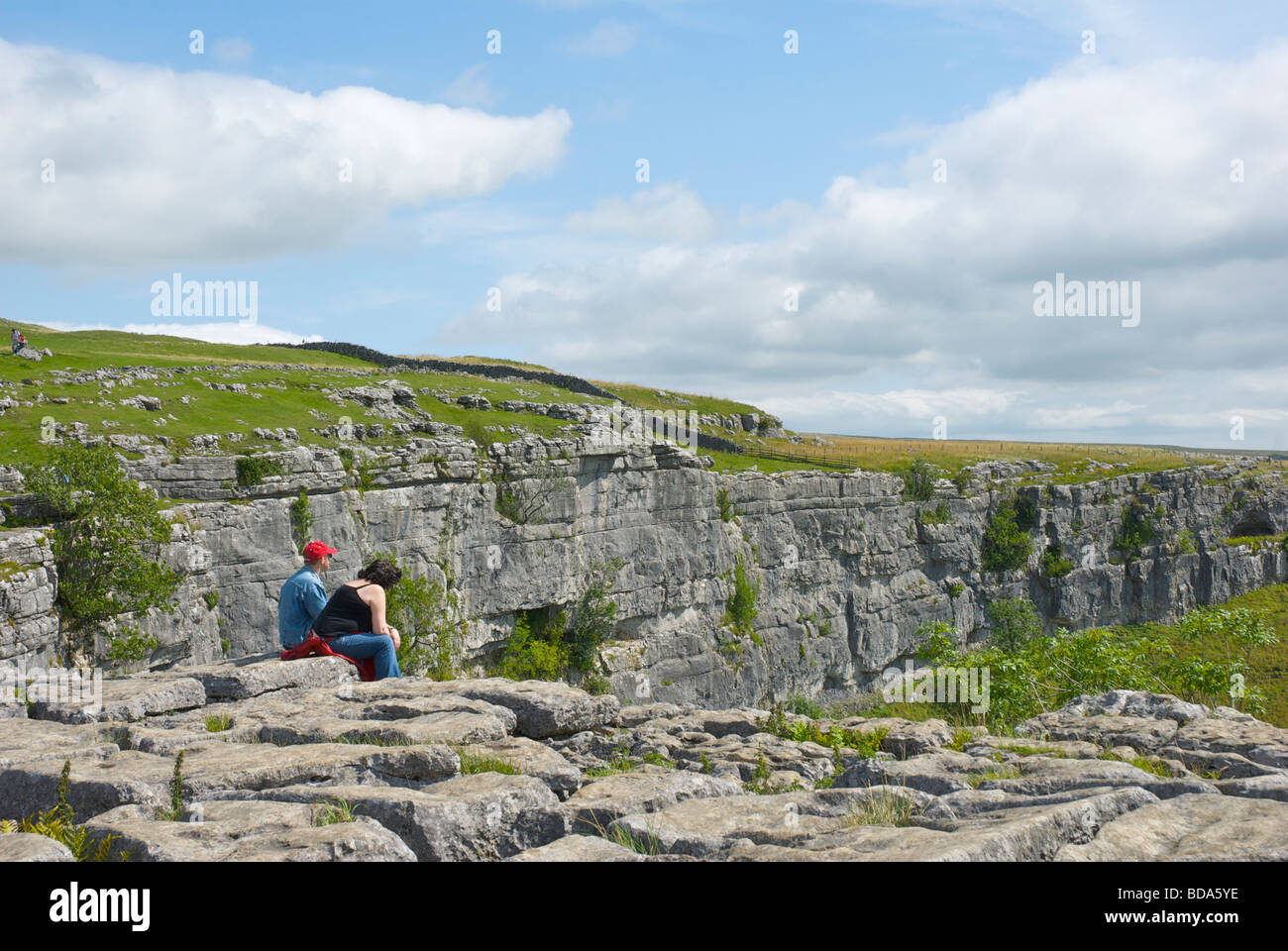 Couple sitting on the limestone pavement on top of Malham Cove ...