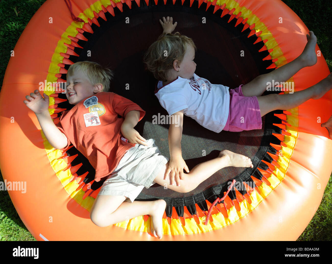 Blond Child Boy and girl Jumping on orange Trampoline in Yard Stock ...