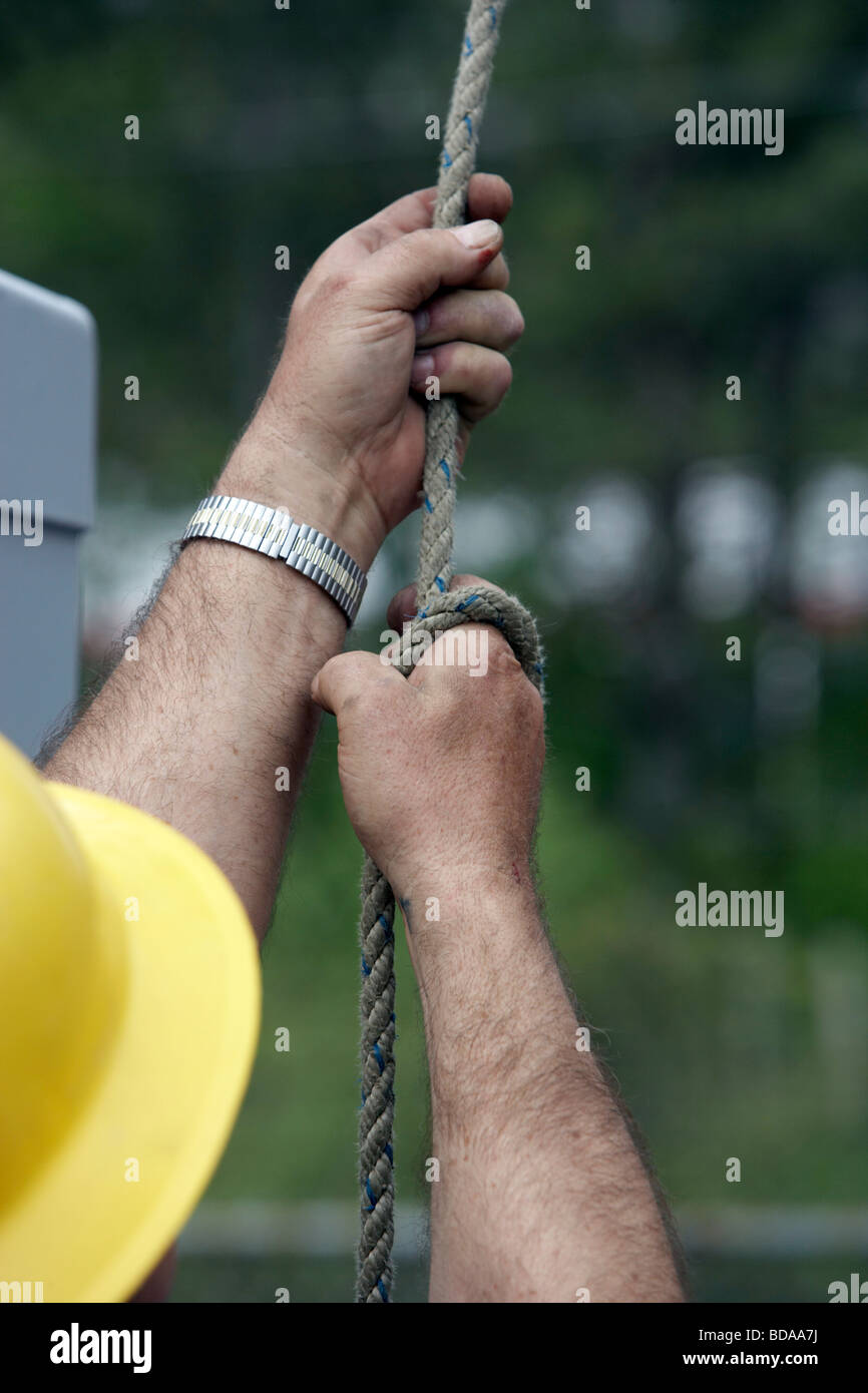 Electrical utility workman wearing a hard hat hauls on a safety line on ...