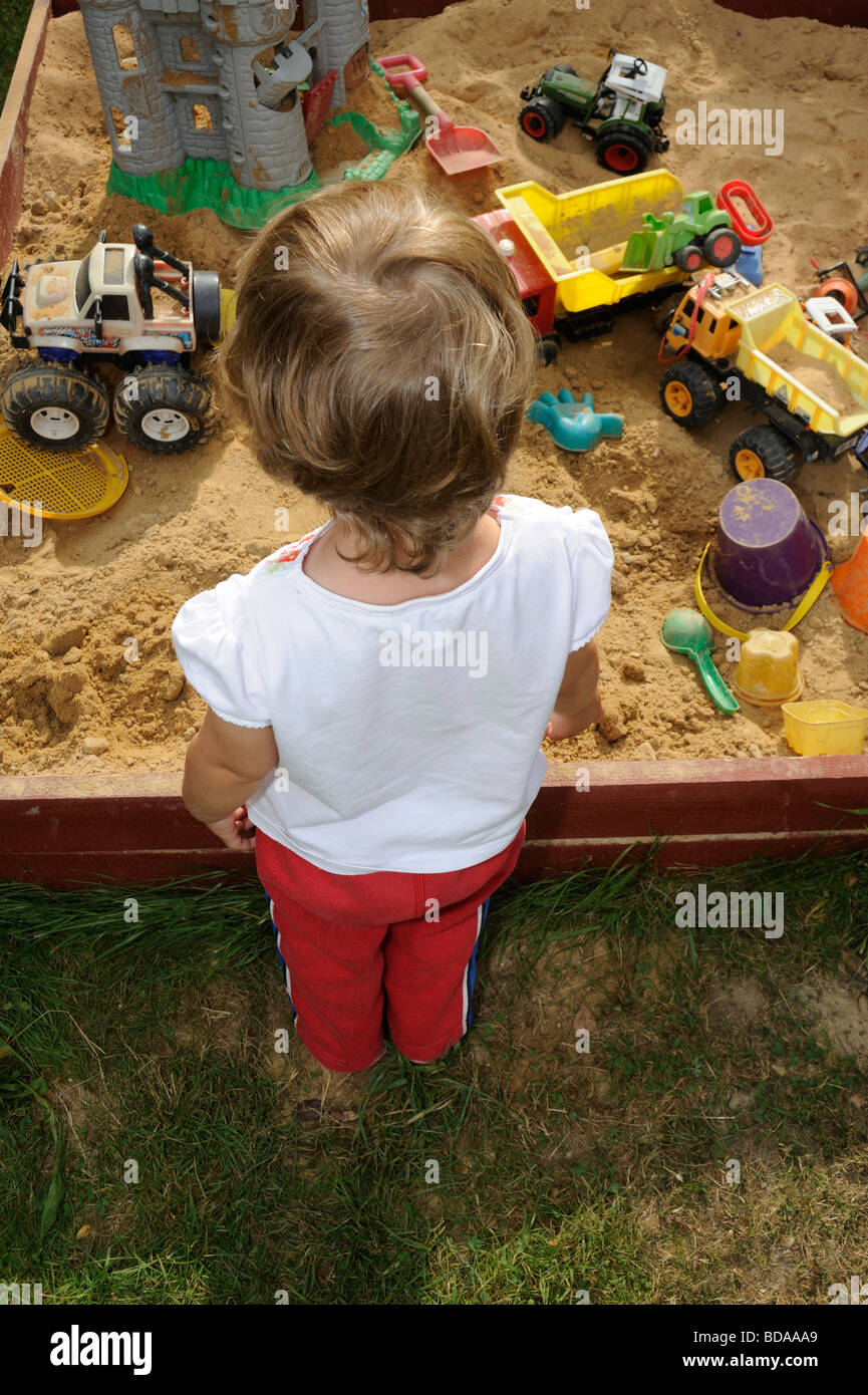 child girl in sand pit playing with spade and toys car cars vehicle ...