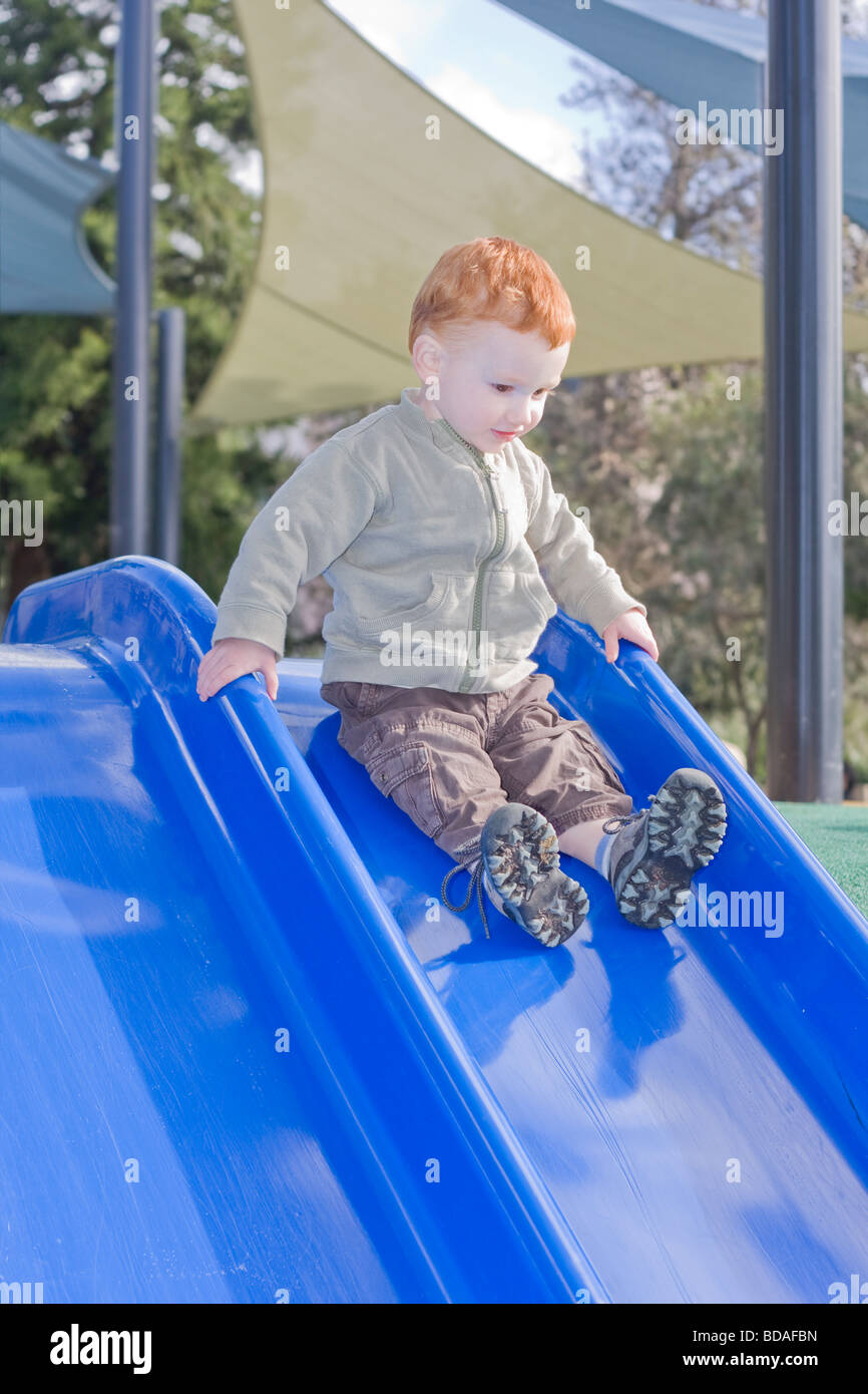 Boy sliding down slide with playground background Stock Photo - Alamy