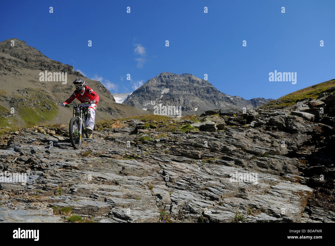 A downhill mountain biker rides down rocks high in the mountains above ...