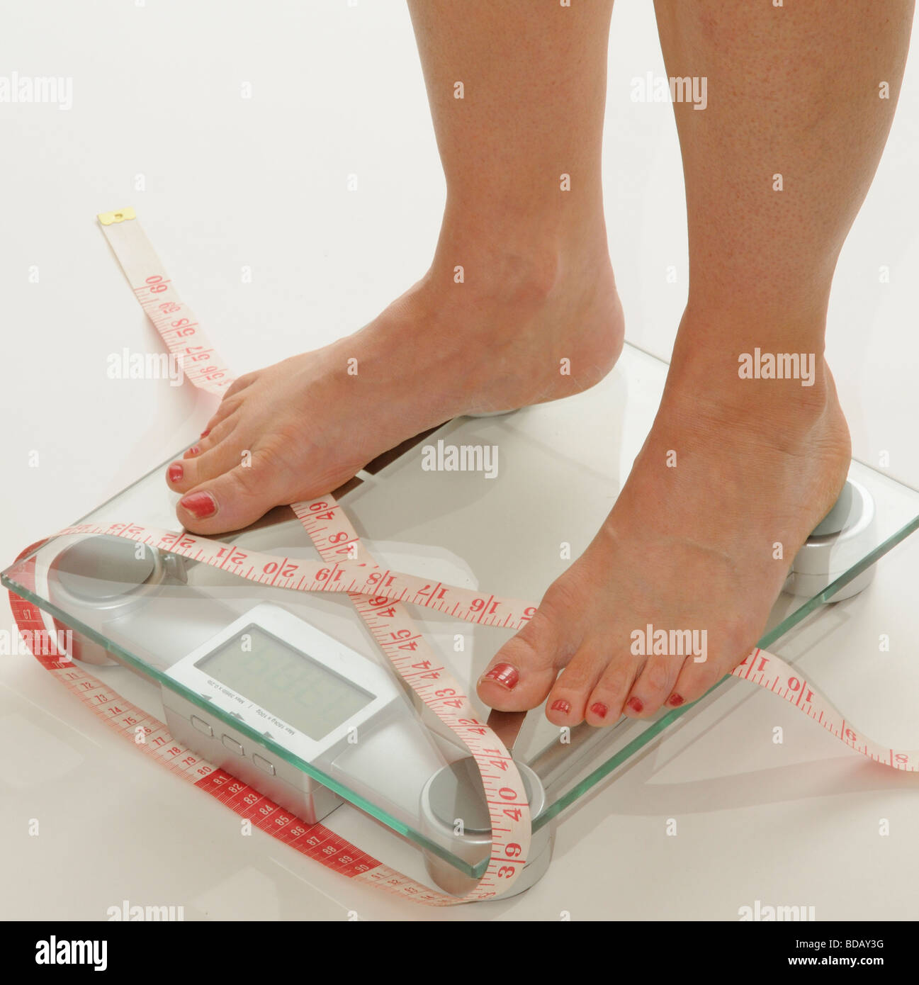 female legs and feet on bathroom scales draped with a tape measure ...