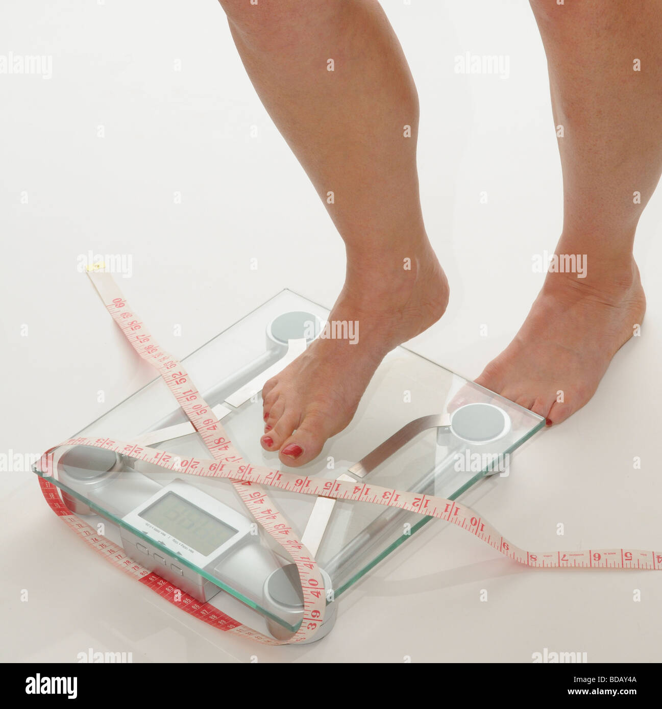 female legs and feet on bathroom scales draped with a tape measure ...