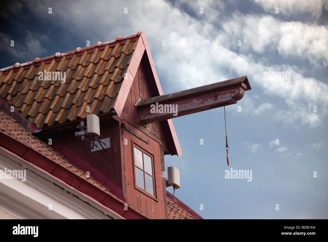 Lifting construction on old house roof with small window and cloudy sky ...