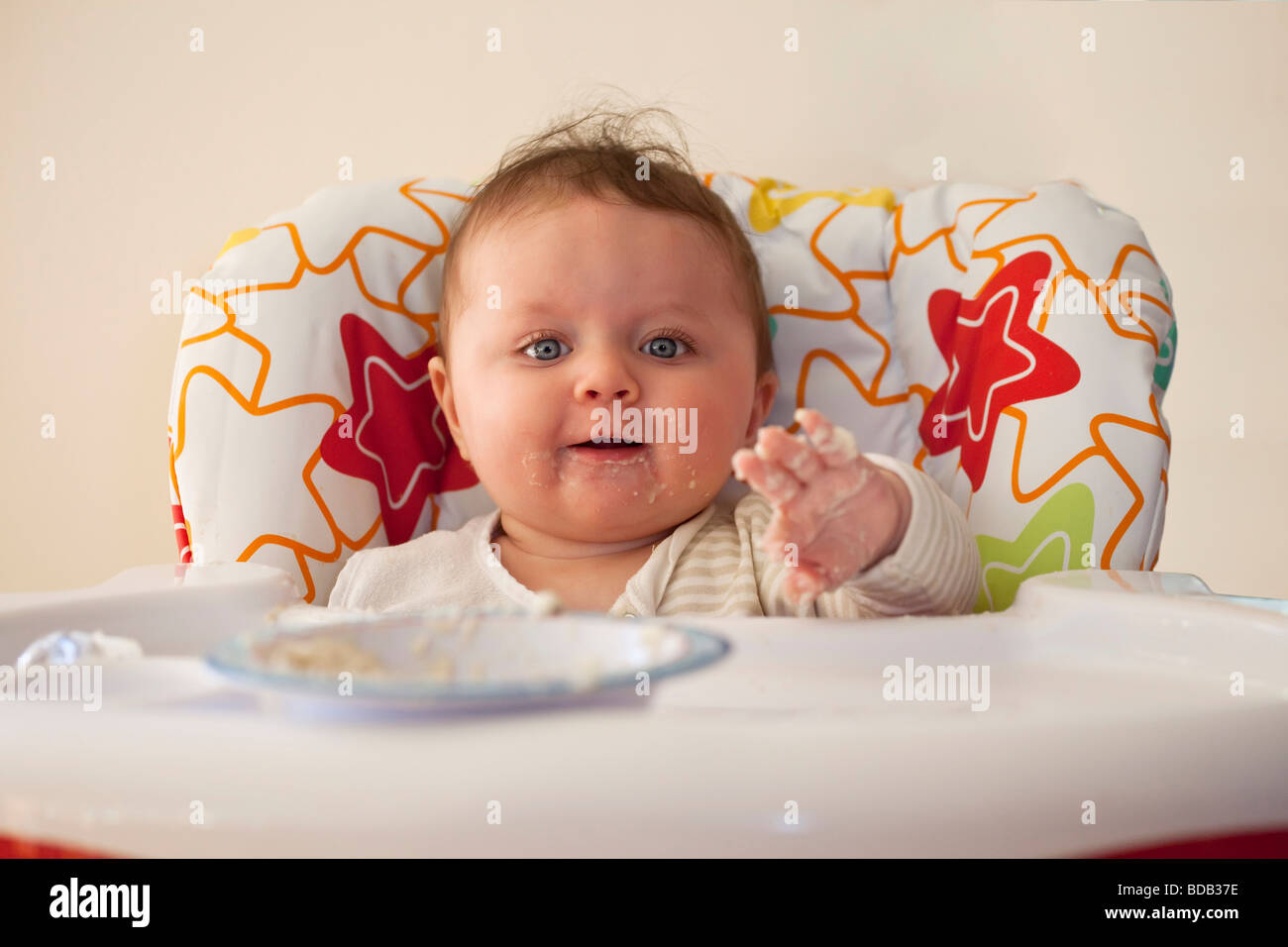 young baby under one year old making a mess with food while trying to ...