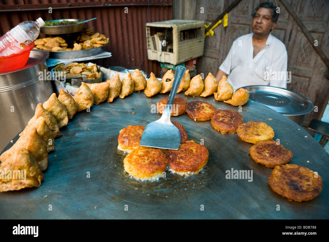 An Indian street seller fries samosas and bhajis on a shallow frying ...