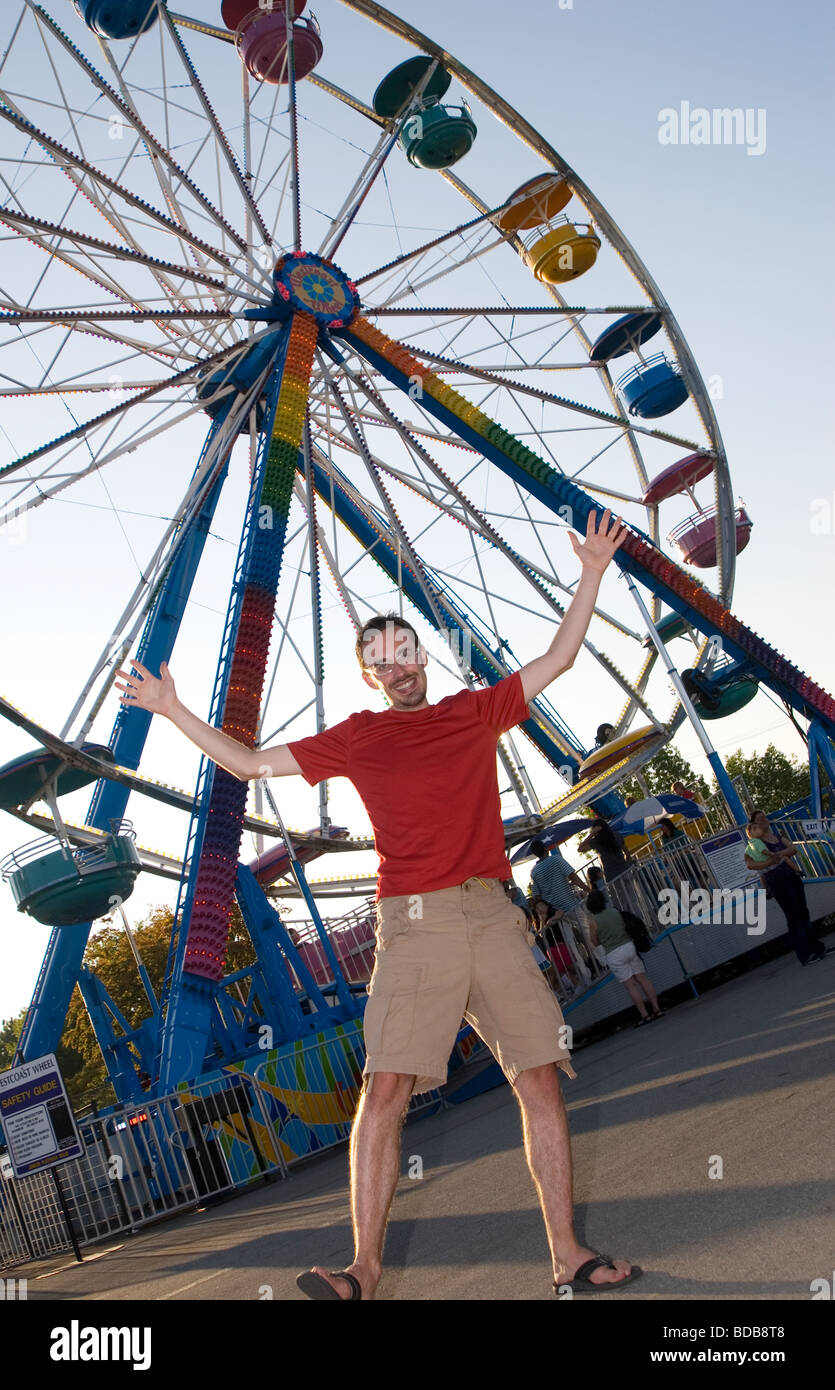 Excited young man standing beside ferris wheel at amusement park Stock ...