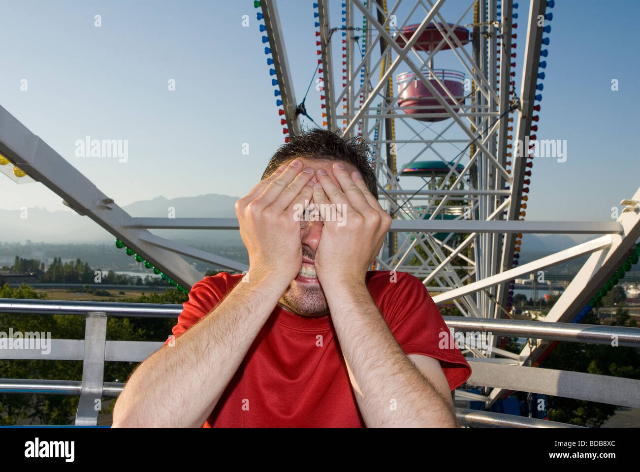 Man on ferris wheel, with his hands covering his eyes Stock Photo - Alamy