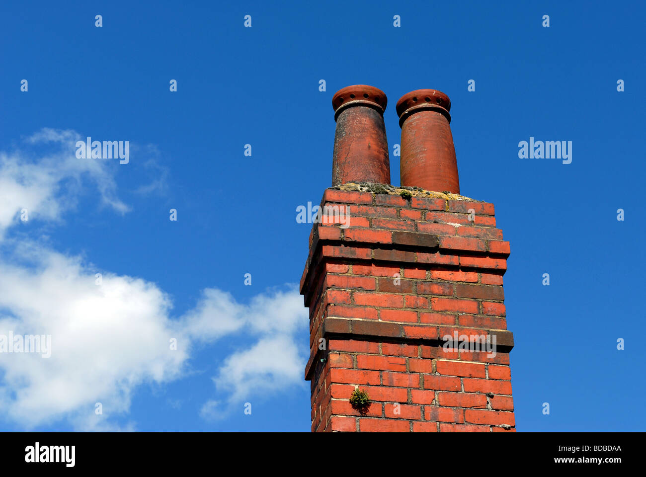 brick chimney stack against a bright blue sky with fluffy white whispy ...