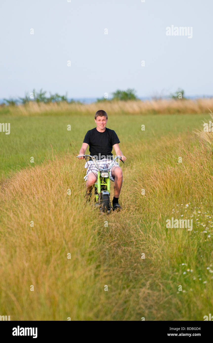 Boy driving a moped in a field by the sea Stock Photo - Alamy