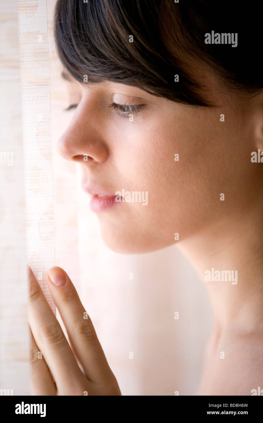 portrait of young woman looking through window Stock Photo - Alamy