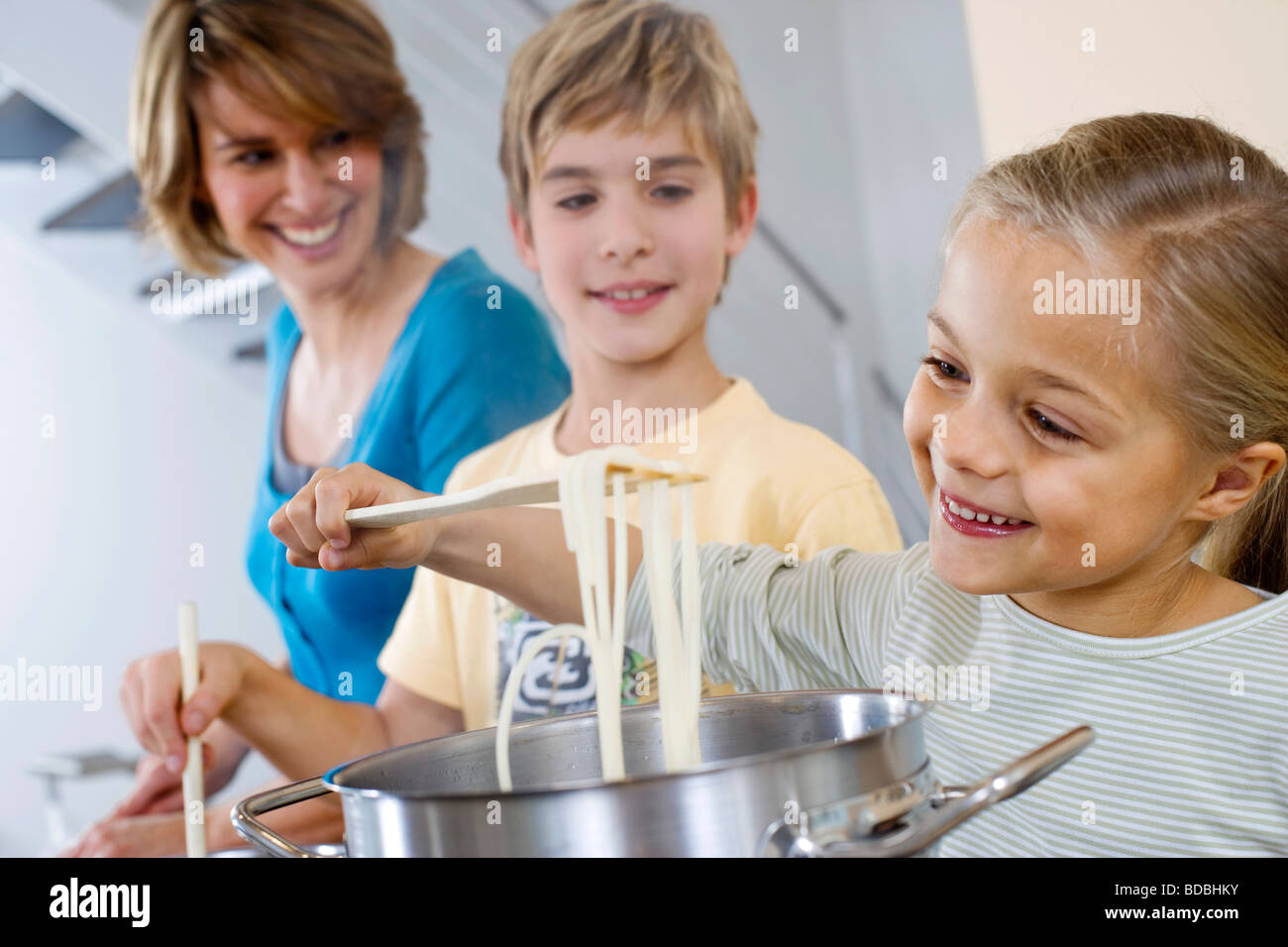 mother and brother watching young girl cooking spaghetti Stock Photo ...