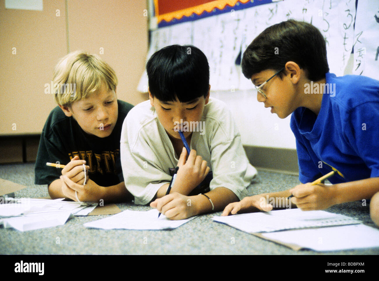 Three boys of different ethnicities lying on the classroom floor ...