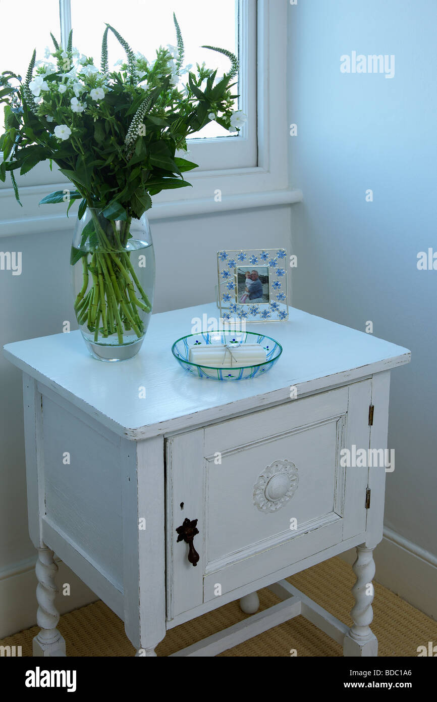 Close up of flowers in glass vase on small white painted cupboard in ...