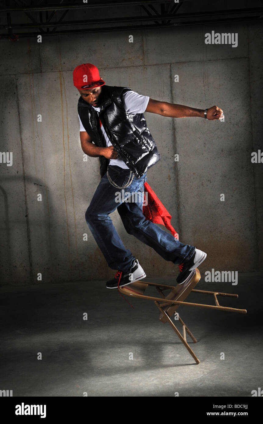 Hip hop dancer performing falling on chair over industrial background ...