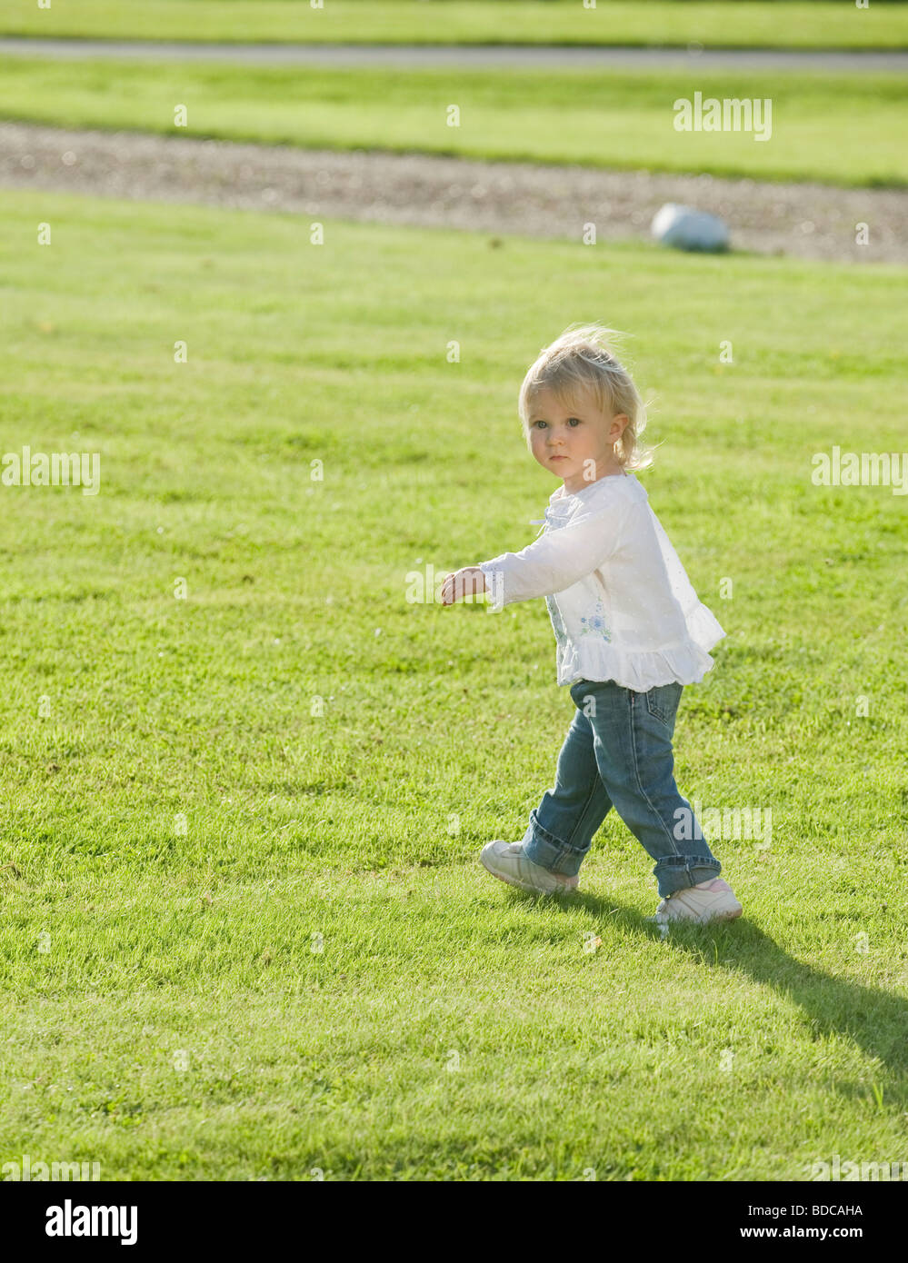 Baby girl toddler striding across grass in summer sunshine Stock Photo ...