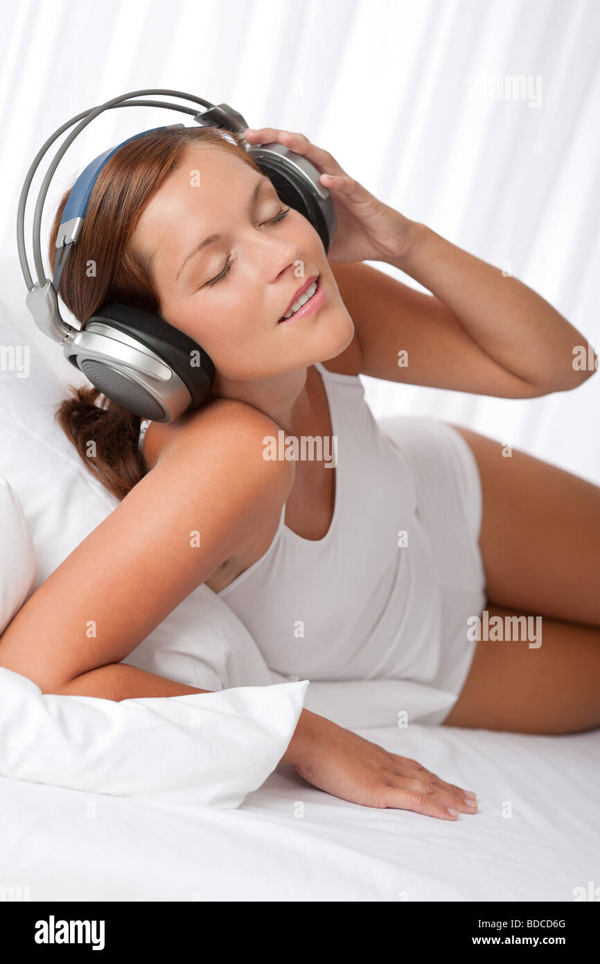 Young Woman In White With Headphones Listening To Music In Bedroom